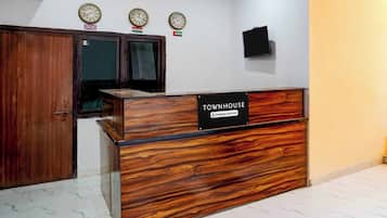 Bancada de recepção com placa indicando serviço da empresa, um armário de madeira e três relógios na parede.