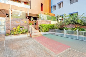 Um edifício moderno com escadaria que leva a uma entrada com portão, cercado por vegetação e céu claro.