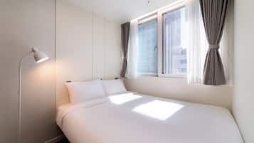 Quarto de hotel com cama, luminária de mesa e janela com cortinas.