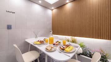 Um lounge moderno com uma mesa branca posta para o café da manhã, incluindo torradas, ovos e frutas.