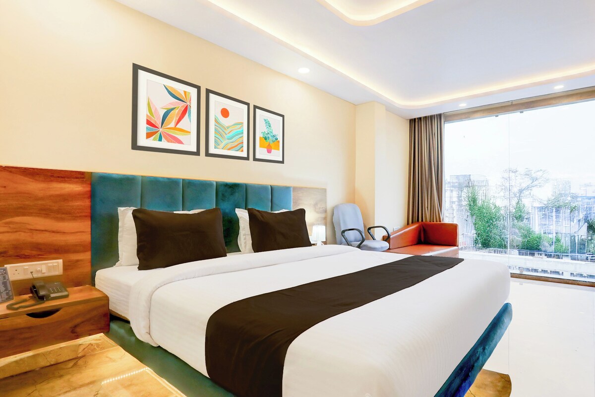 Quarto de hotel com uma cama grande, cabeceira, escrivaninha com telefone e janela com vista.