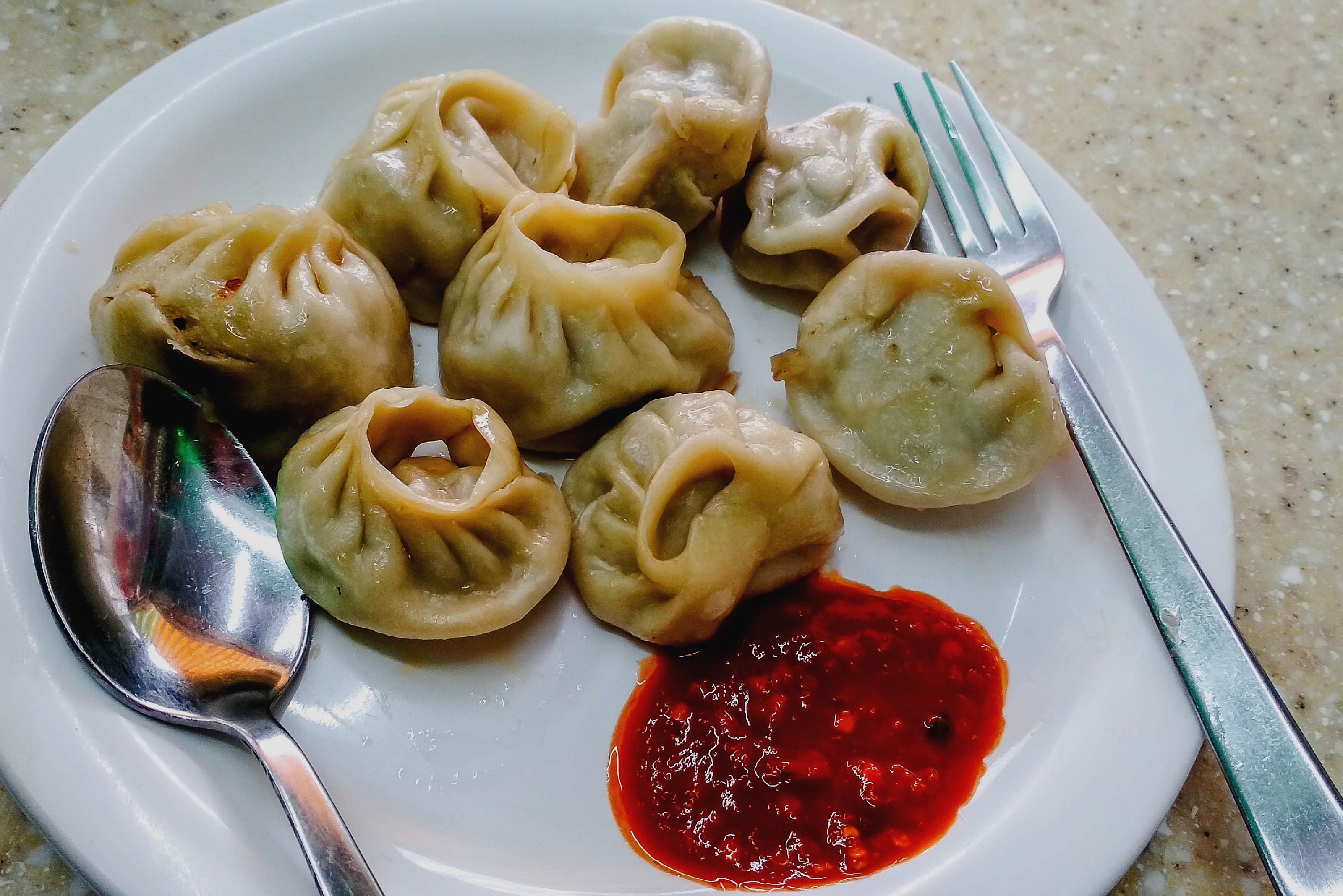 Um prato de dumplings com um garfo e uma colher, e uma tigela pequena de molho vermelho.