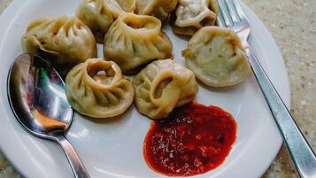 Um prato de dumplings com um garfo e uma colher, e uma tigela pequena de molho vermelho.