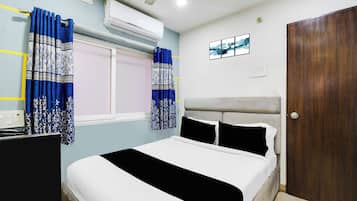 Quarto com cama, janela com cortinas, ar condicionado, porta e interruptor de luz fixado na parede.