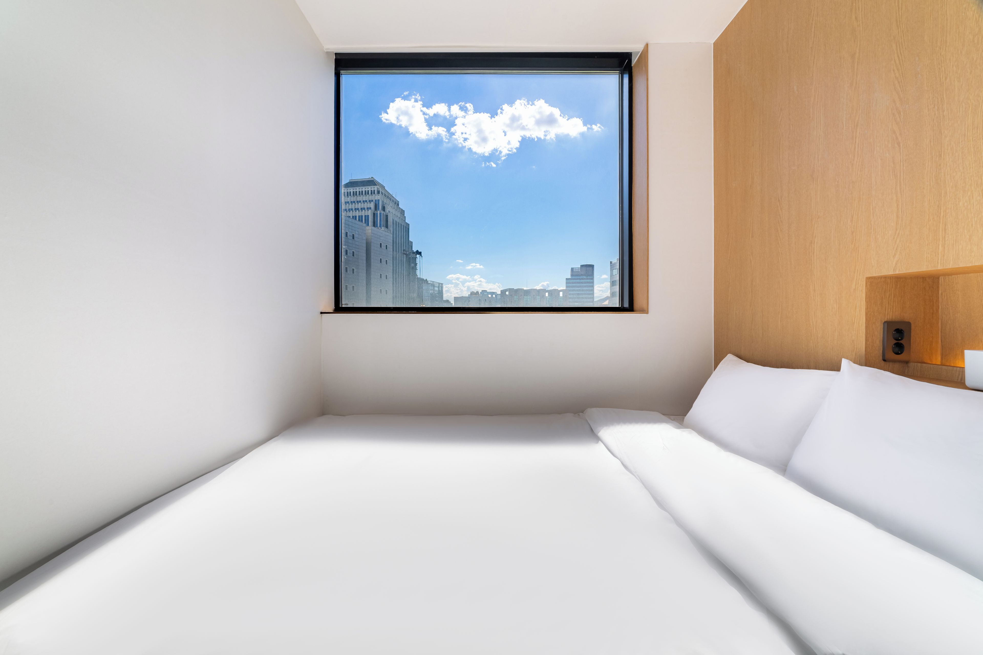 Quarto de hotel com uma janela grande, uma cama e cabeceira de madeira.