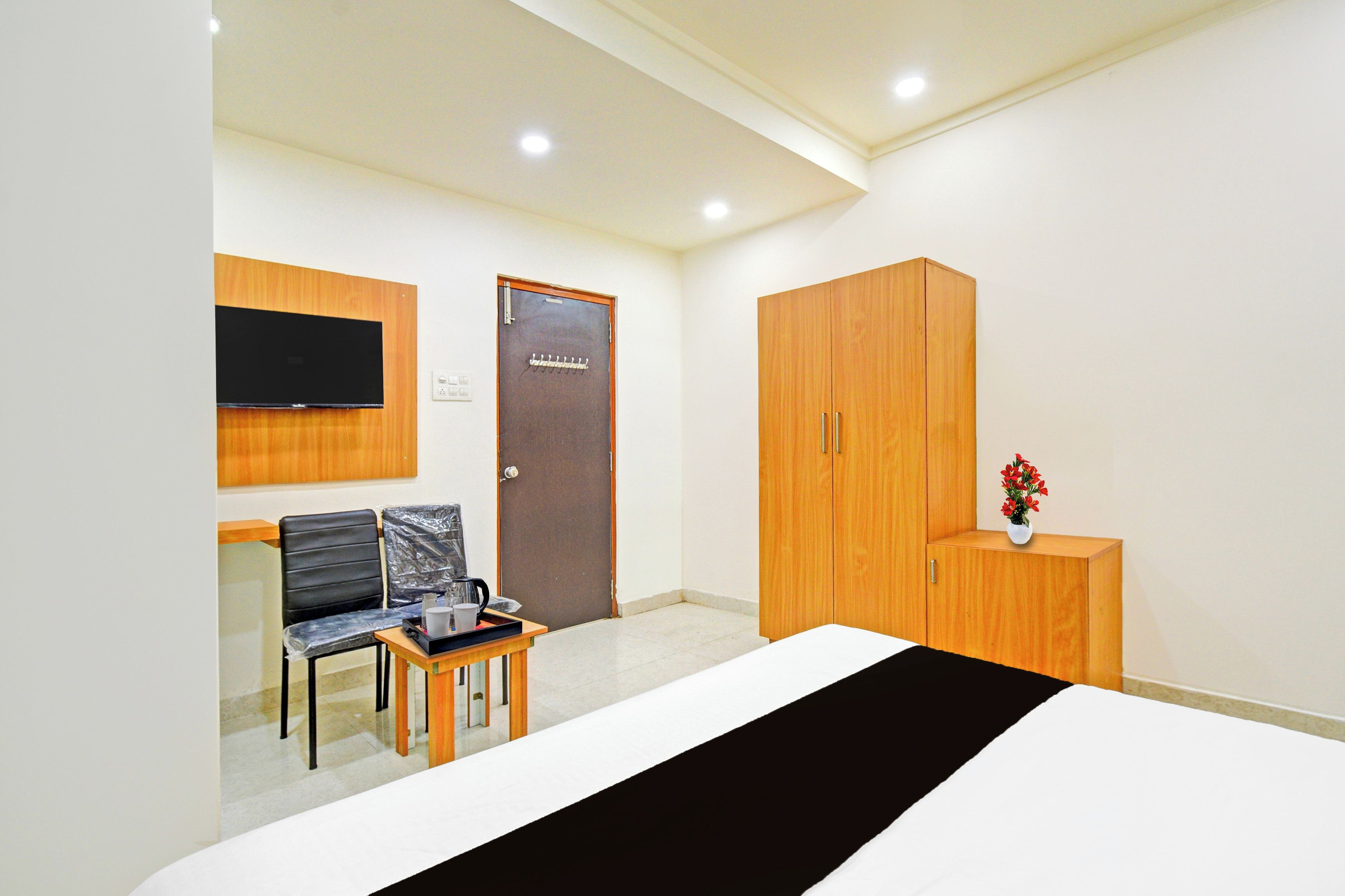Quarto de hotel com cama, escrivaninha, cadeira, guarda-roupa e televisão na parede.
