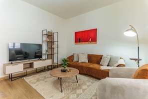 Uma sala de estar moderna com televisão de tela plana, sofá, mesa de centro e um quadro na parede.
