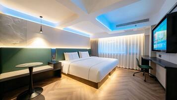 Quarto de hotel moderno com cama, escrivaninha, cadeira, televisão e vista para o exterior.