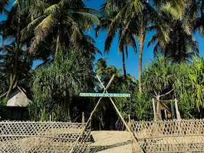 Placa indicando JUKUTIR ECO RESORT, com cerca de bambu e palmeiras ao fundo.