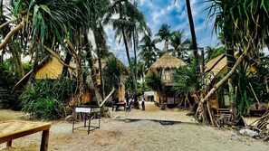 Um resort tropical com cabanas de palha, palmeiras e chão arenoso.