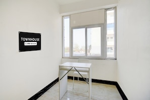 Um quarto com uma mesa branca e uma janela, um letreiro na parede e vista externa.