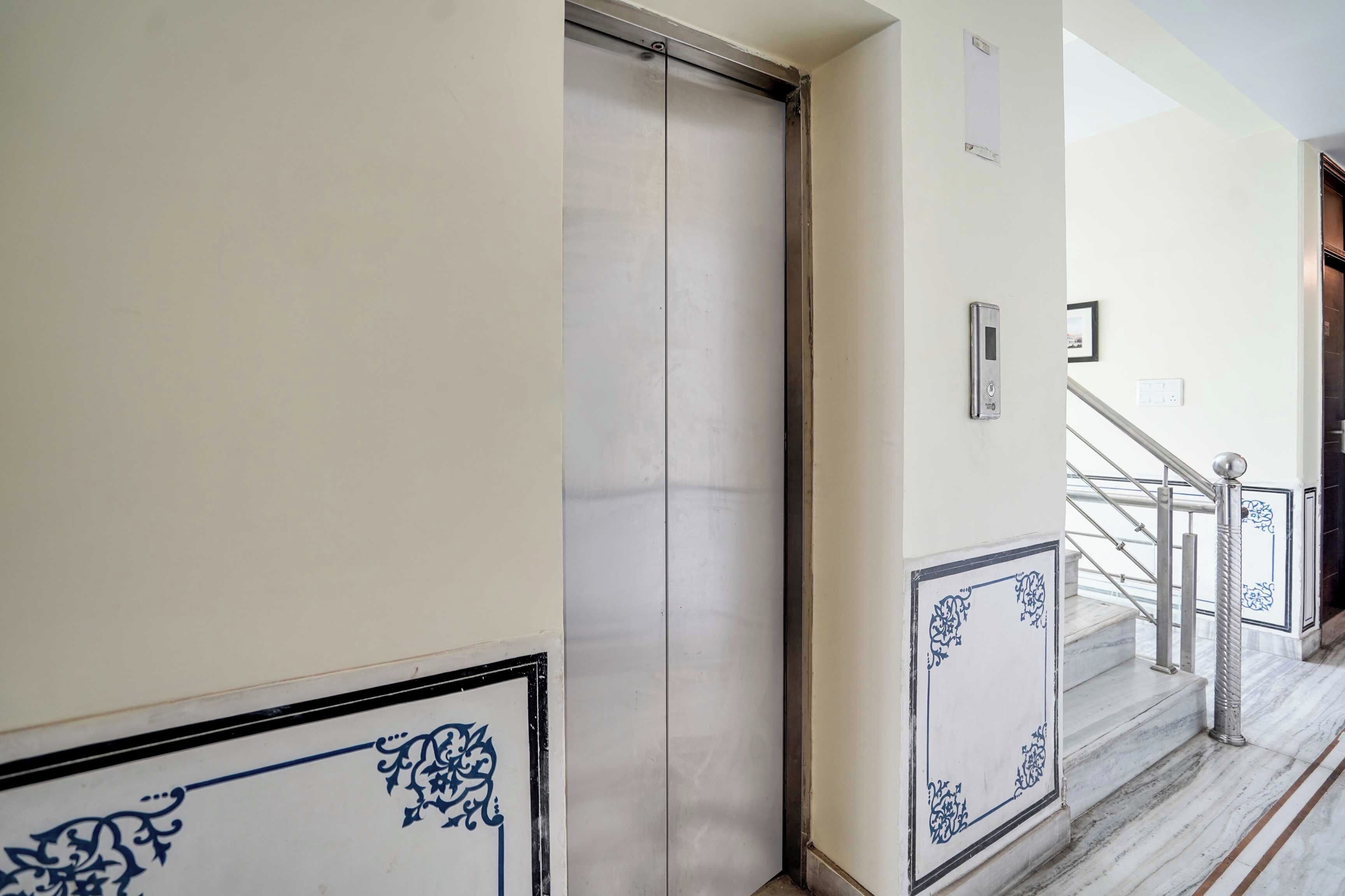 Corredor com elevador fechado, interfone na parede e escada com corrimão de metal.
