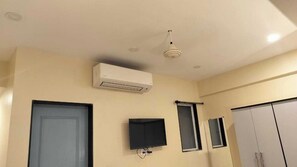 Quarto com televisão de tela plana na parede, ar condicionado instalado no teto, porta e guarda-roupa.