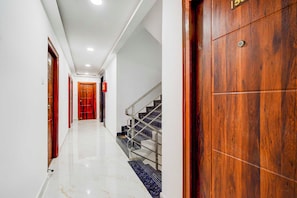 Um corredor com piso de mármore, portas de madeira e escada com corrimão de metal.