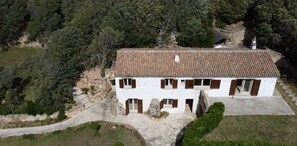 Um edifício branco com telhado em cerâmica, rodeado por árvores e um espaço pavimentado.