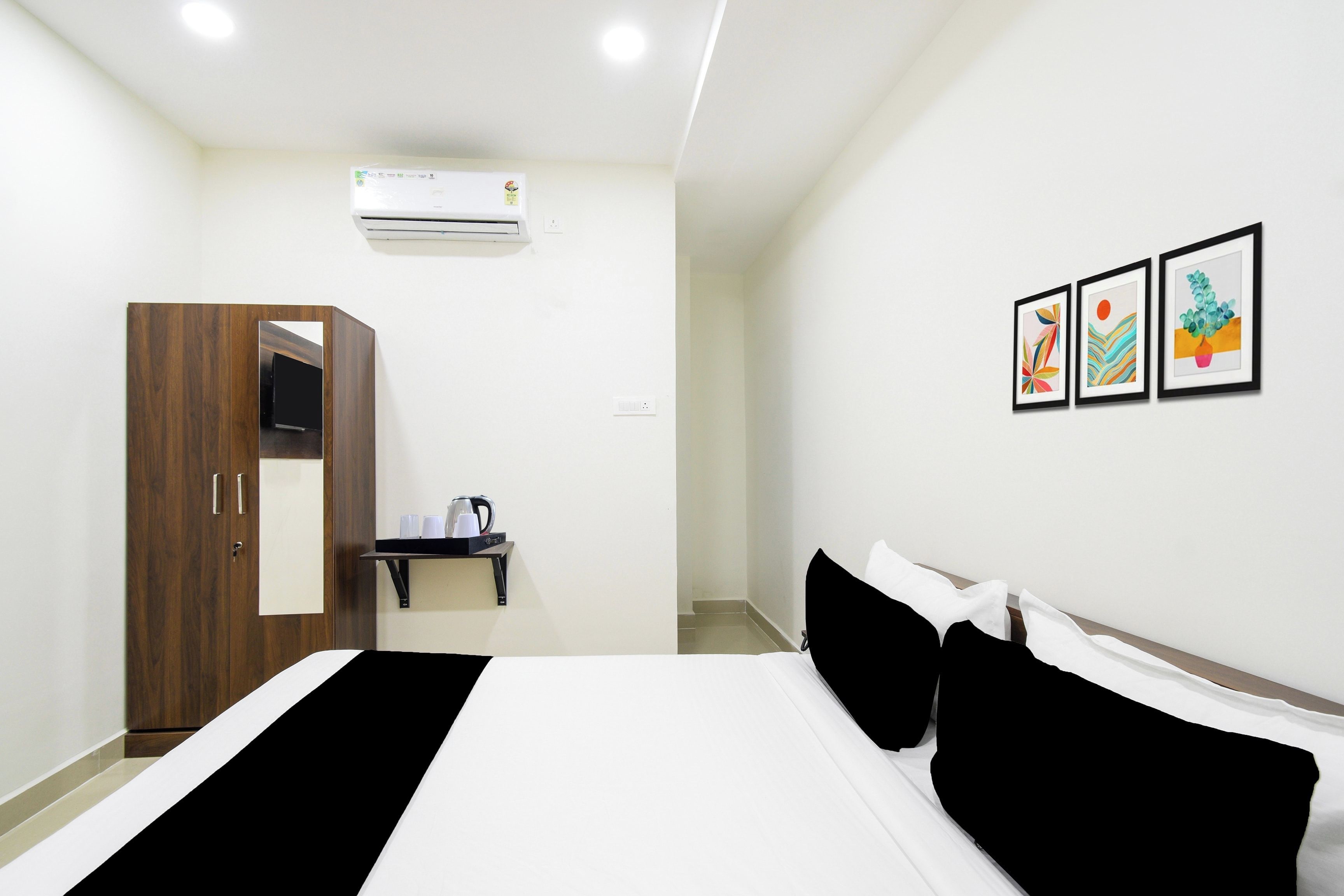 Quarto de hotel com cama, guarda-roupa, uma mesinha com chaleira e três obras de arte emolduradas na parede.