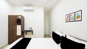 Quarto de hotel com cama, guarda-roupa, uma mesinha com chaleira e três obras de arte emolduradas na parede.