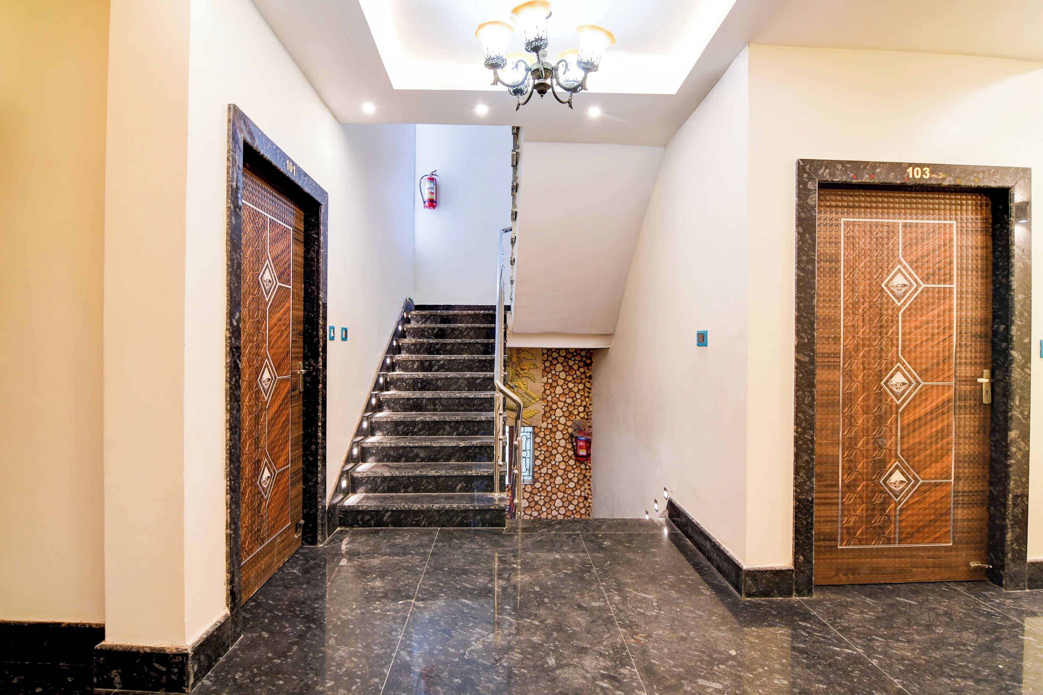 Um corredor com piso de mármore, uma escadaria e duas portas ricamente decoradas.