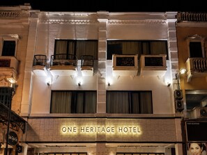 Fachada de hotel com placa indicando 'ONE HERITAGE HOTEL'.