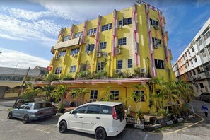 Edifício amarelo de vários andares com varandas, carros estacionados e céu aberto.
