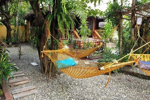 Uma rede instalada entre árvores em um jardim, com uma estrutura de telhado de palha ao fundo.