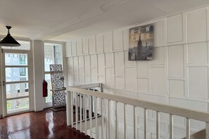 Corredor com painéis brancos, escada com corrimão branco e uma obra de arte com paisagem urbana na parede.
