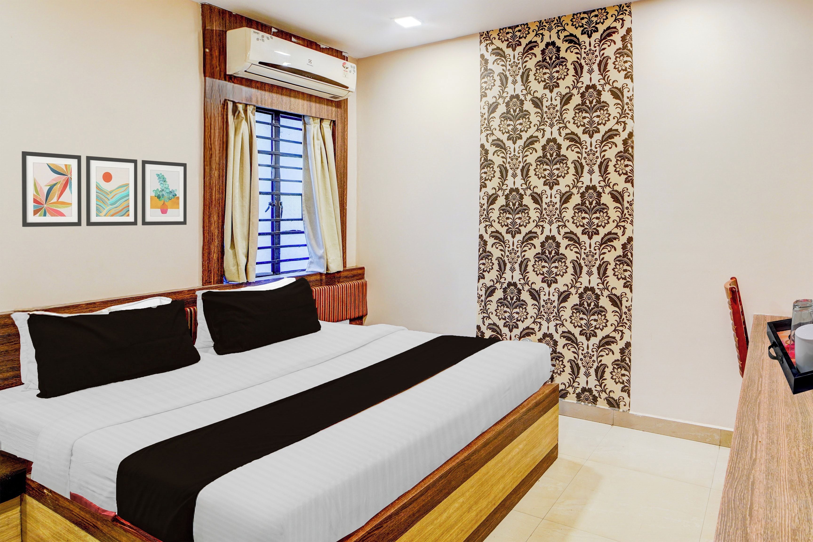 Quarto de hotel com cama, ar condicionado, janela com cortinas e parede com obras de arte emolduradas.
