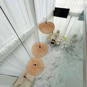 Interior moderno com mesa de jantar de vidro, cortinas brancas e televisão de tela plana.