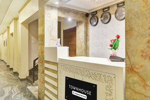 Uma área de recepção de hotel com um balcão de mármore, relógios mostrando diferentes fusos horários e uma placa indicando que o estabelecimento é de serviço corporativo.