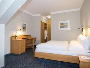 Quarto de hotel com cama, escrivaninha, cadeira e armário.