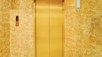 Um elevador dourado em um corredor com paredes de mármore e um botão de chamada digital.