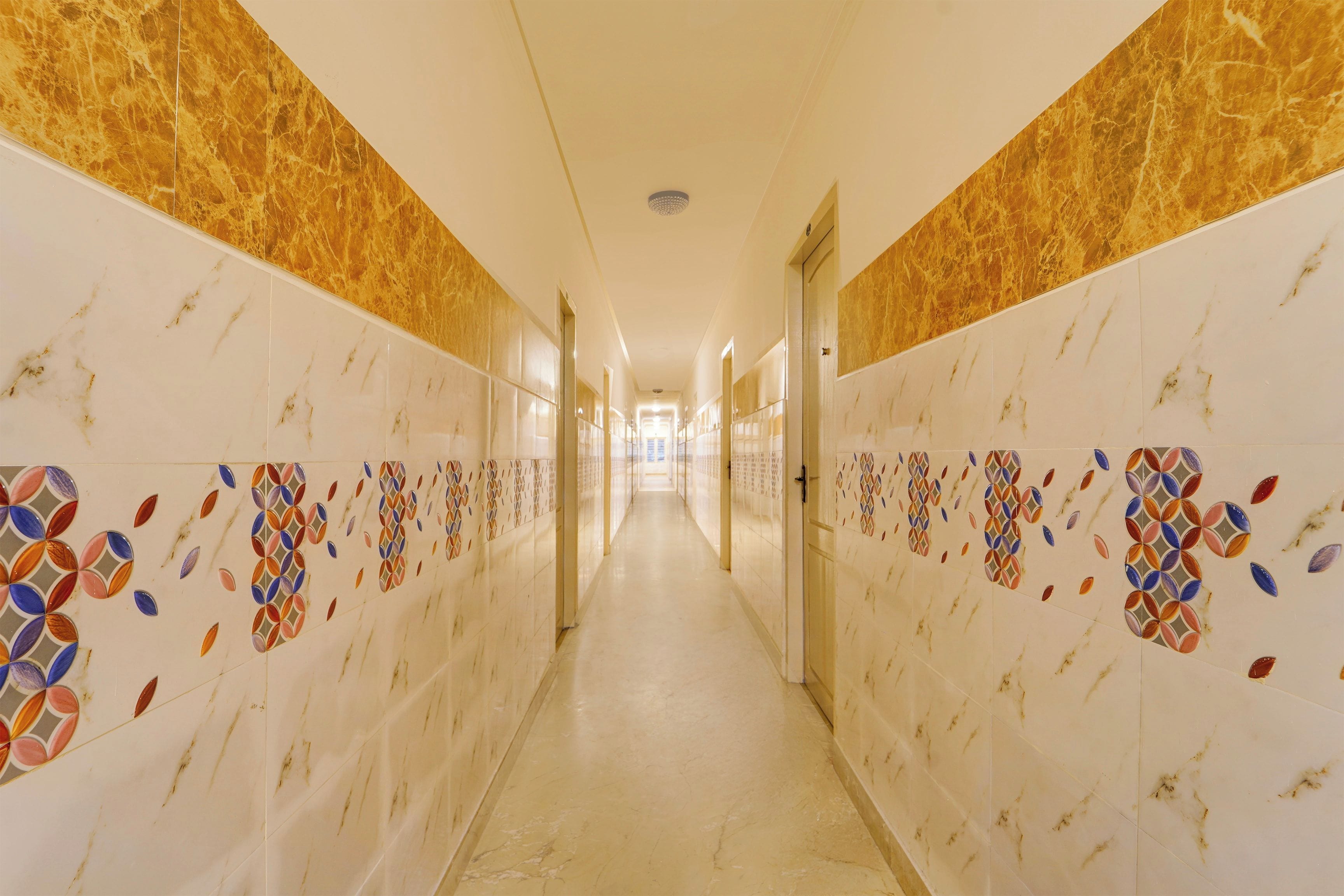 Corredor de hotel com paredes de mármore e azulejos estampados, que conduz a um quarto claro no final.