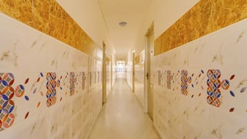 Corredor de hotel com paredes de mármore e azulejos estampados, que conduz a um quarto claro no final.
