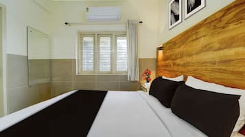 Quarto de hotel com uma cama grande, cabeceira de madeira, janela com cortinas, ar condicionado fixado na parede e um quadro emoldurado na parede.