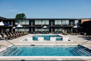 Área de piscina com espreguiçadeiras e guarda-sóis, um edifício com janelas amplas e céu claro.