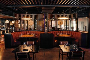 Restaurante com cabines e mesas, detalhes em madeira e iluminação pendente.