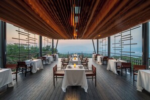 Restaurante com deck de madeira, toalhas de mesa brancas e vista para as montanhas.