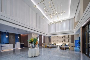 Um lobby espaçoso com teto alto, luminárias modernas e área de estar com sofás e mesas redondas.