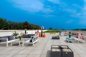 Terraço no telhado com área de estar ao ar livre, vista para o oceano e um edifício ao fundo.