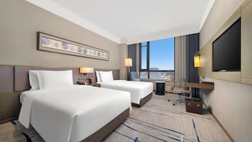 Quarto de hotel com duas camas, uma escrivaninha, uma cadeira, televisão e vista para a cidade.