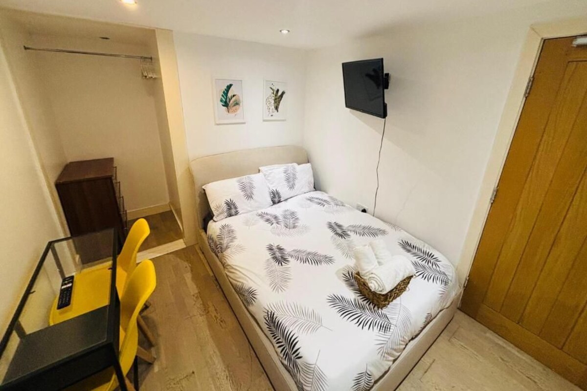 Quarto com cama, escrivaninha, cadeira, televisão e porta.