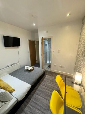 Quarto com uma cama, televisão de tela plana na parede, uma cadeira e uma pequena mesa com abajur.