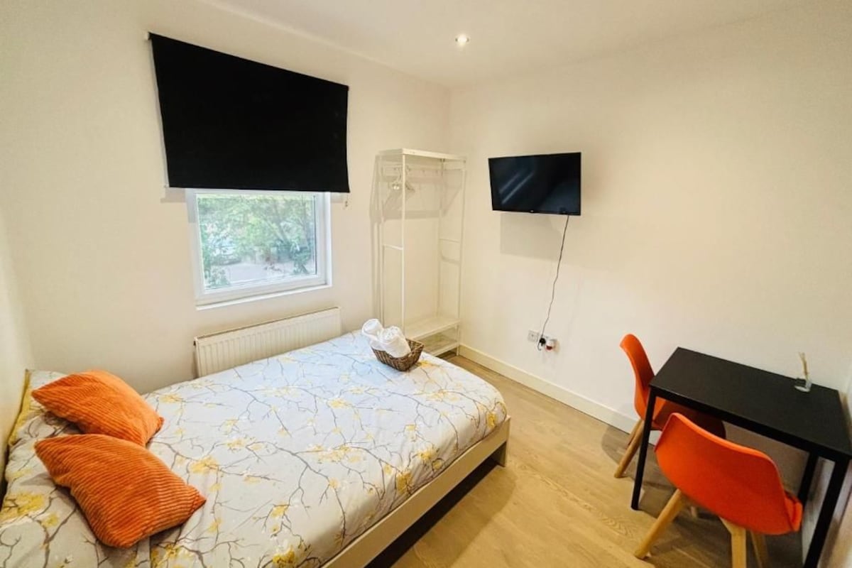 Quarto com cama, escrivaninha, cadeira, televisão e janela.