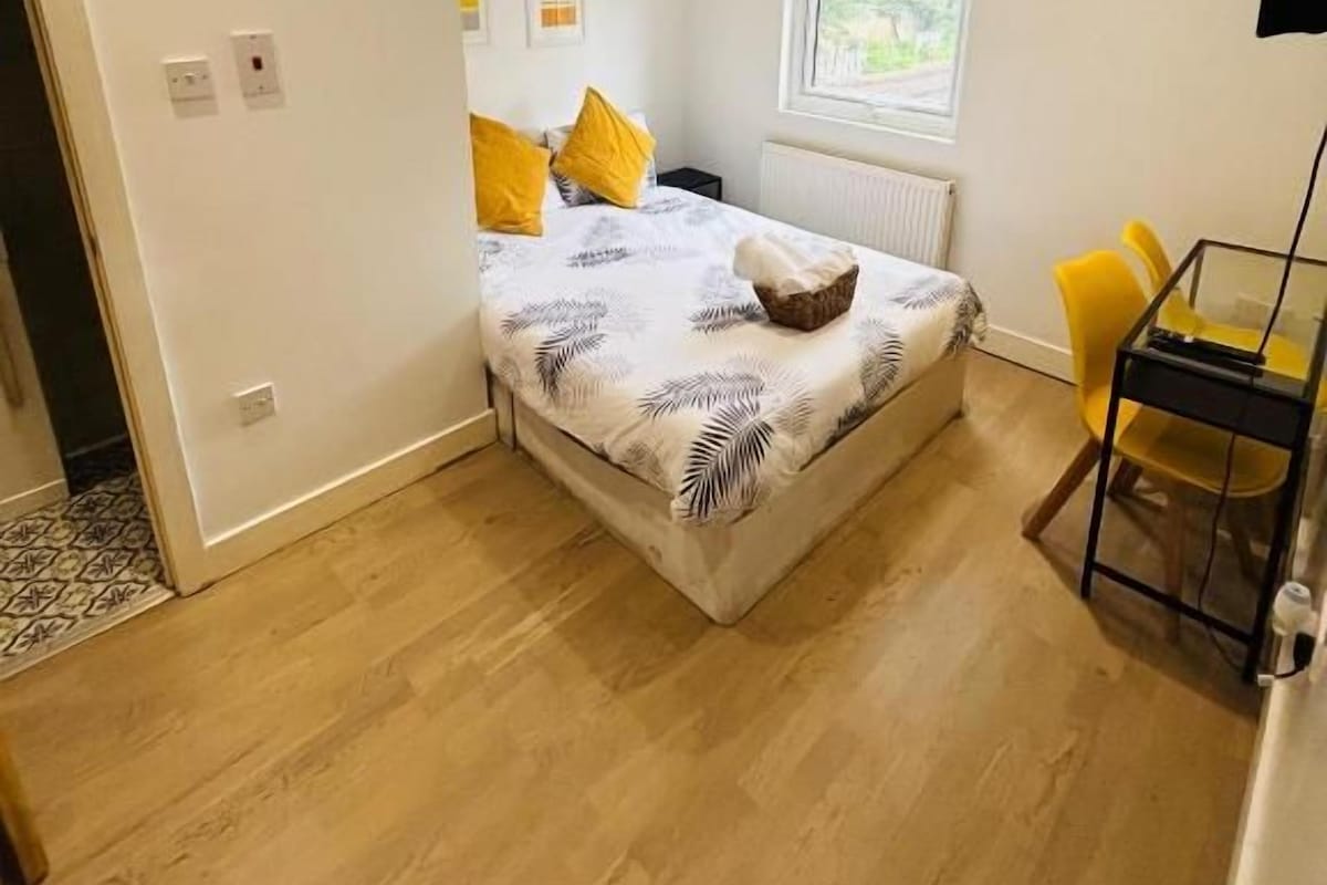 Quarto com cama, janela com persianas, radiador e uma pequena mesa com cadeira.
