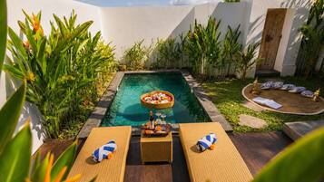 Área de piscina com uma piscina pequena, cadeiras de descanso e espaço para refeições.