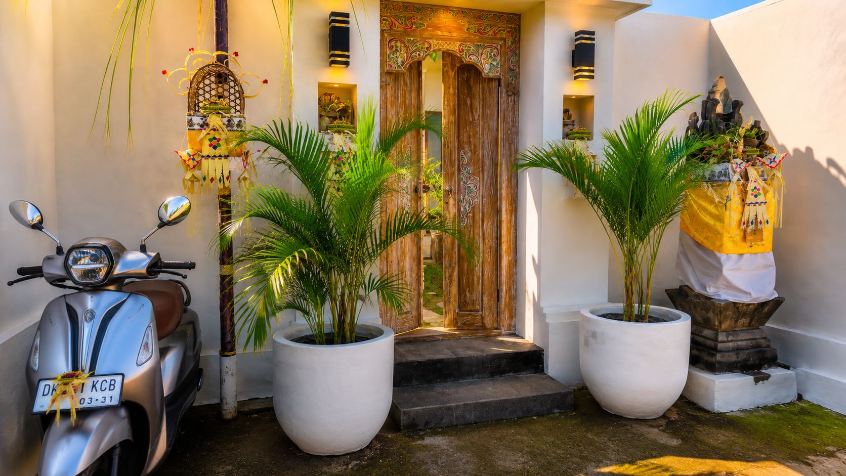 Uma scooter estacionada em frente a um prédio com porta decorativa e plantas em vasos.
