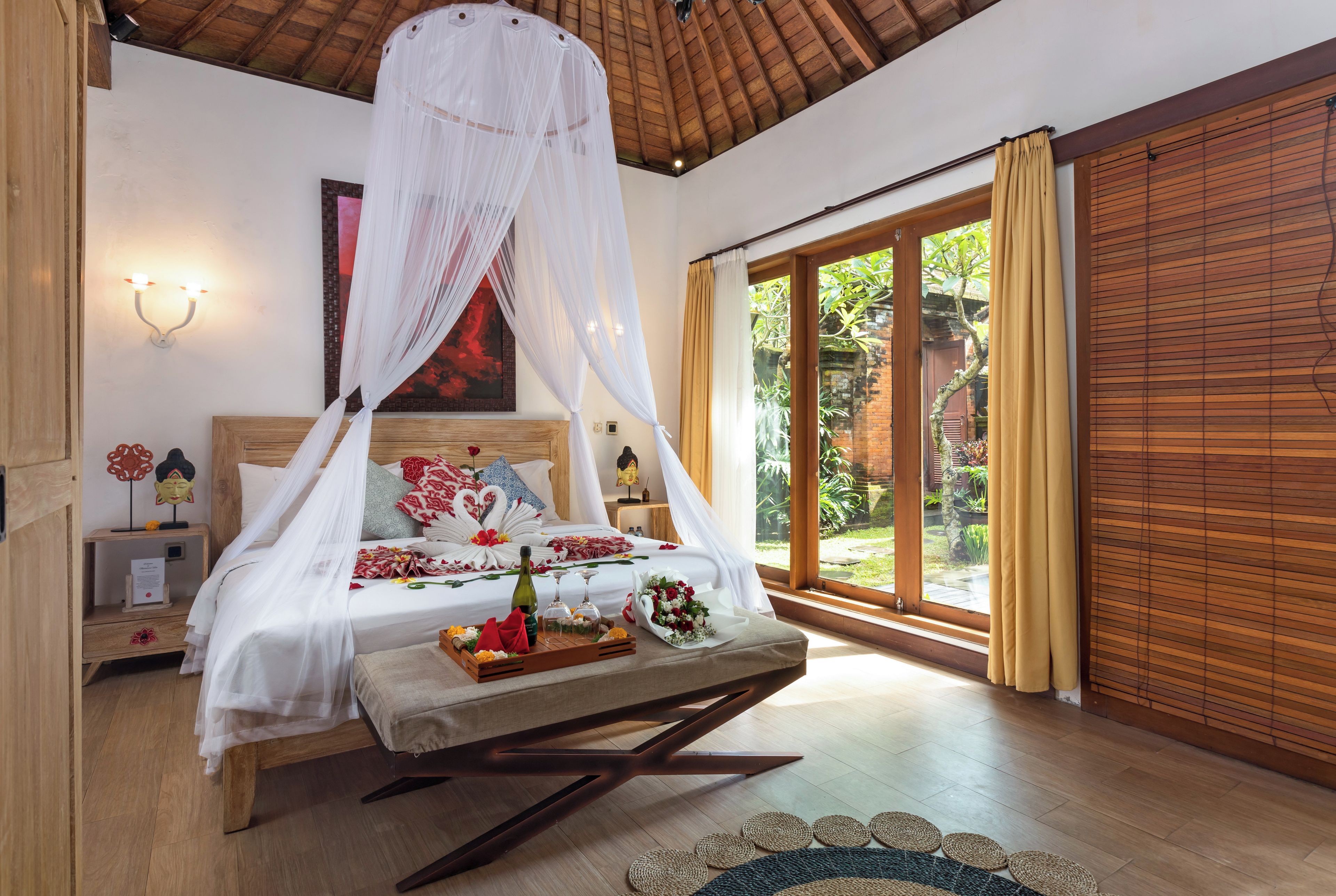 Quarto com cama de dossel, mesas de cabeceira, mesa de apoio e vista para o jardim através de uma porta deslizante.