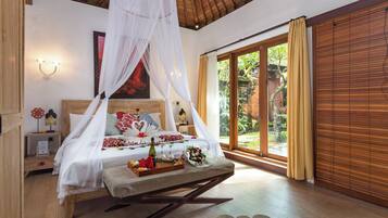 Quarto com cama de dossel, mesas de cabeceira, mesa de apoio e vista para o jardim através de uma porta deslizante.