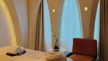 Quarto com cama, uma cadeira e uma pequena mesa com uma planta.