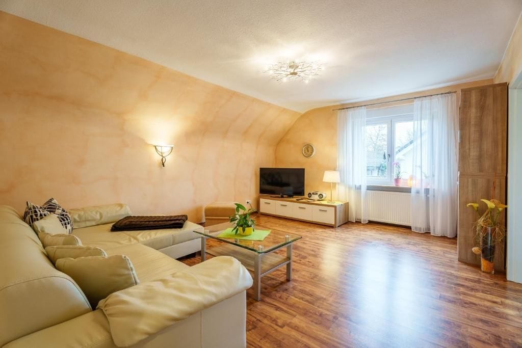 Sala de estar com sofá, mesa de centro de vidro, televisão e janela com cortinas.